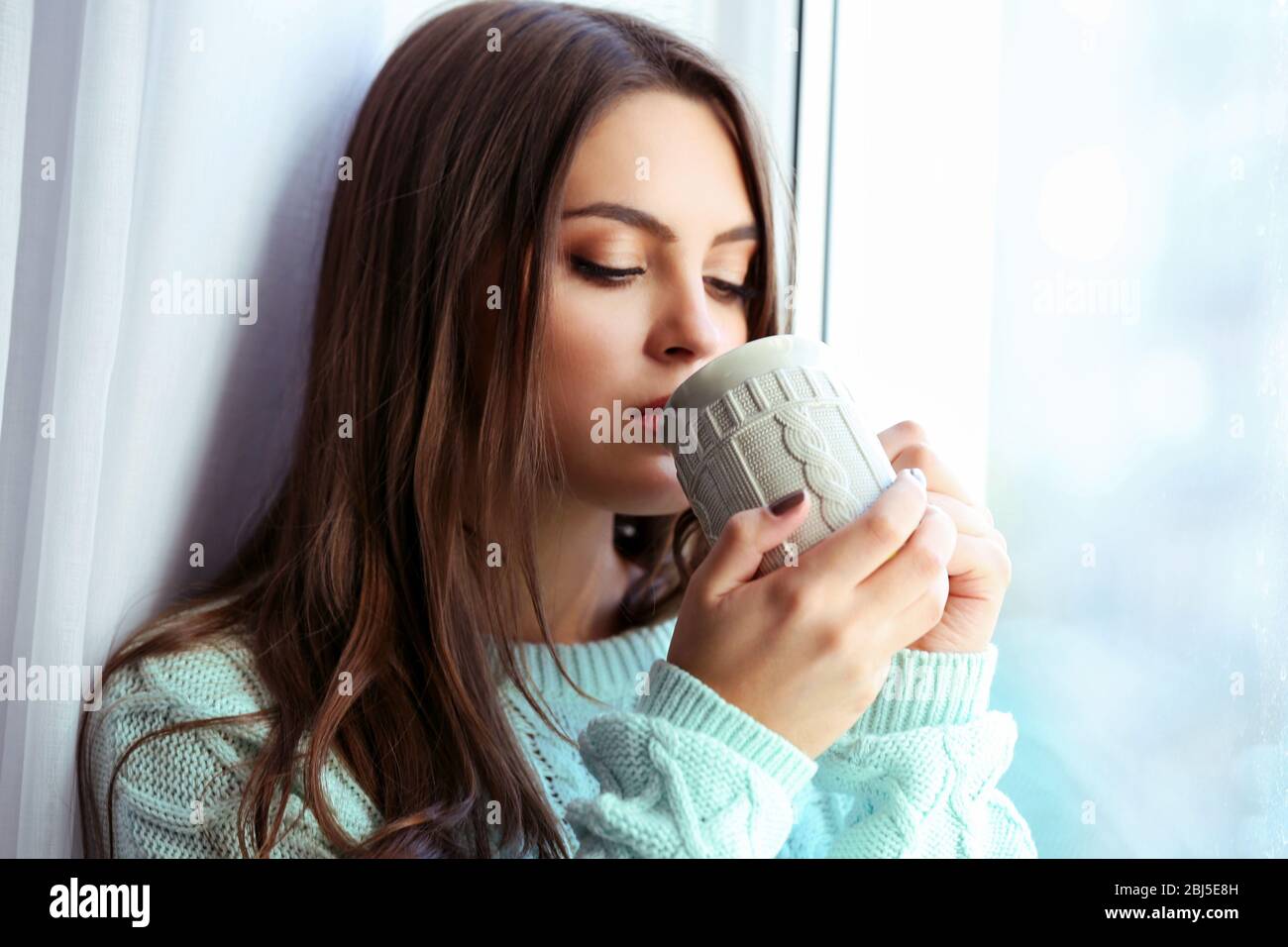 Woman drinking coffee near window in the room Stock Photo - Alamy