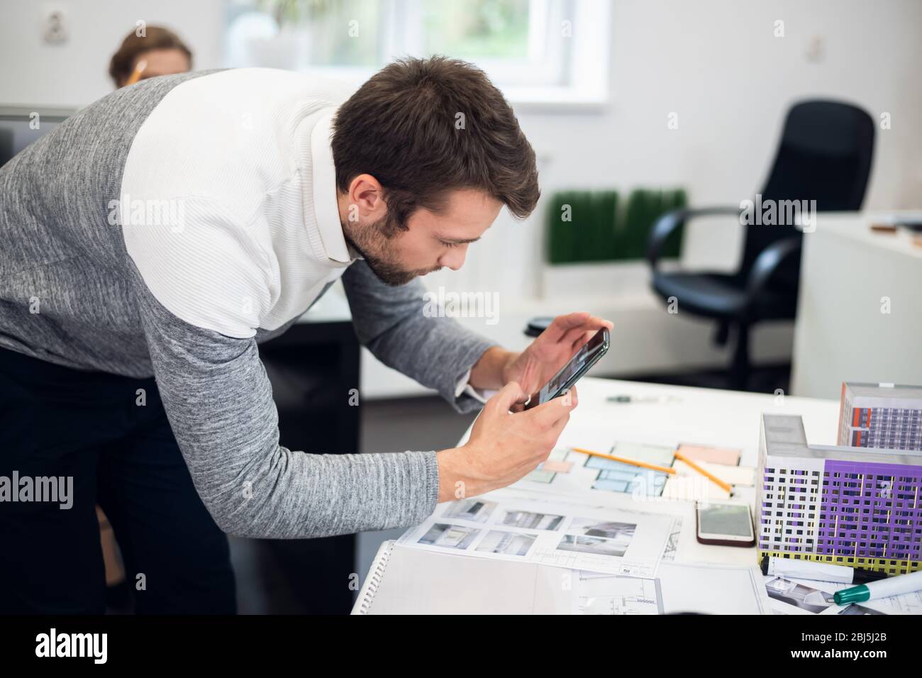 A young architect taking pictures of the construction model while in ...
