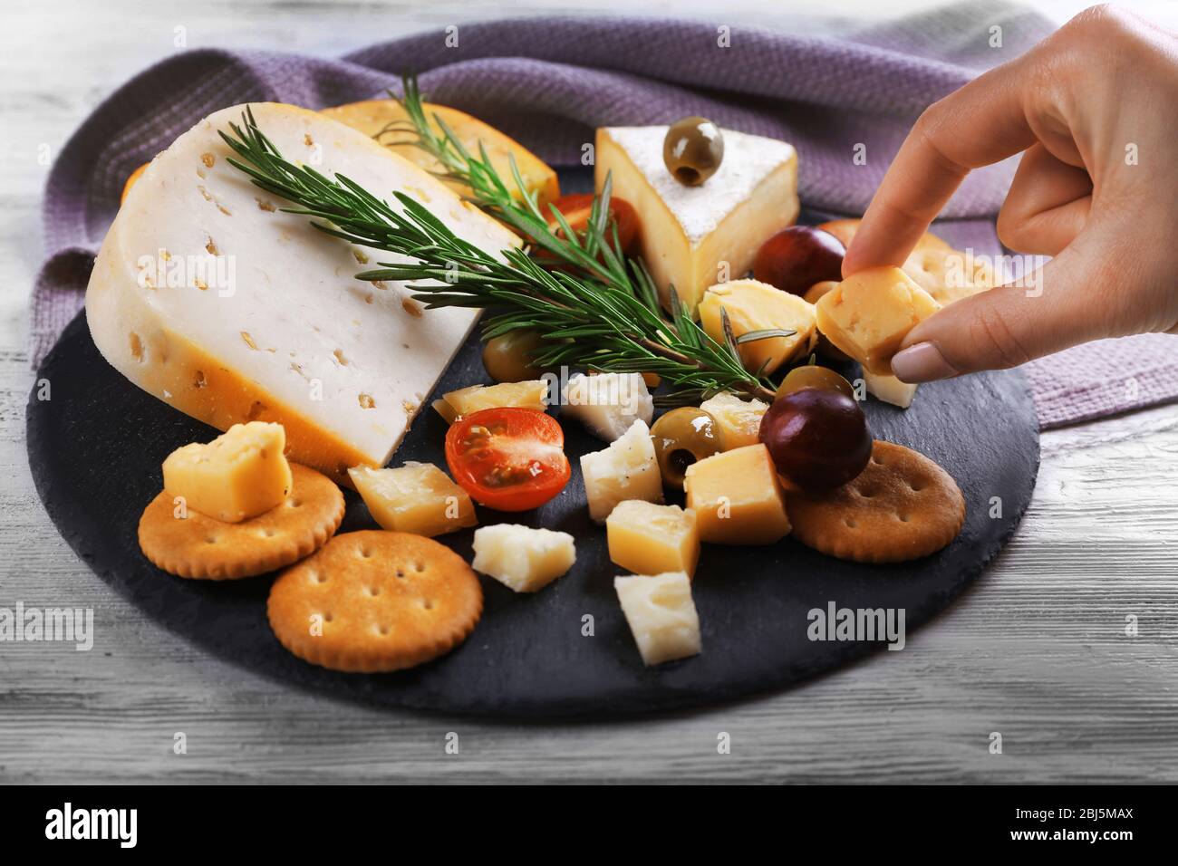 Hand takes peace of cheese from round board with food Stock Photo - Alamy
