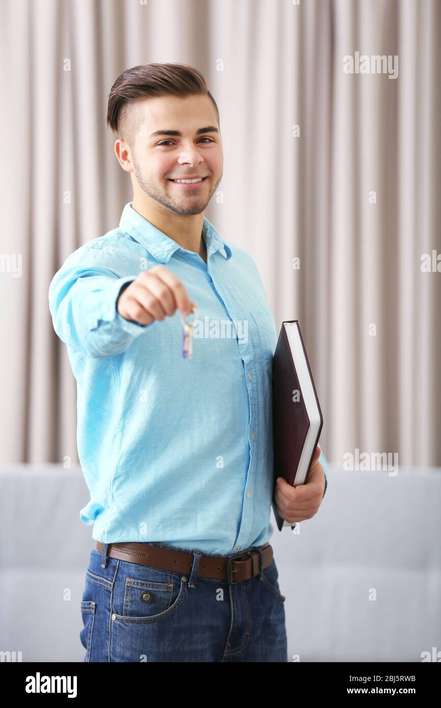 Friendly male estate-agent with key on light background Stock Photo - Alamy