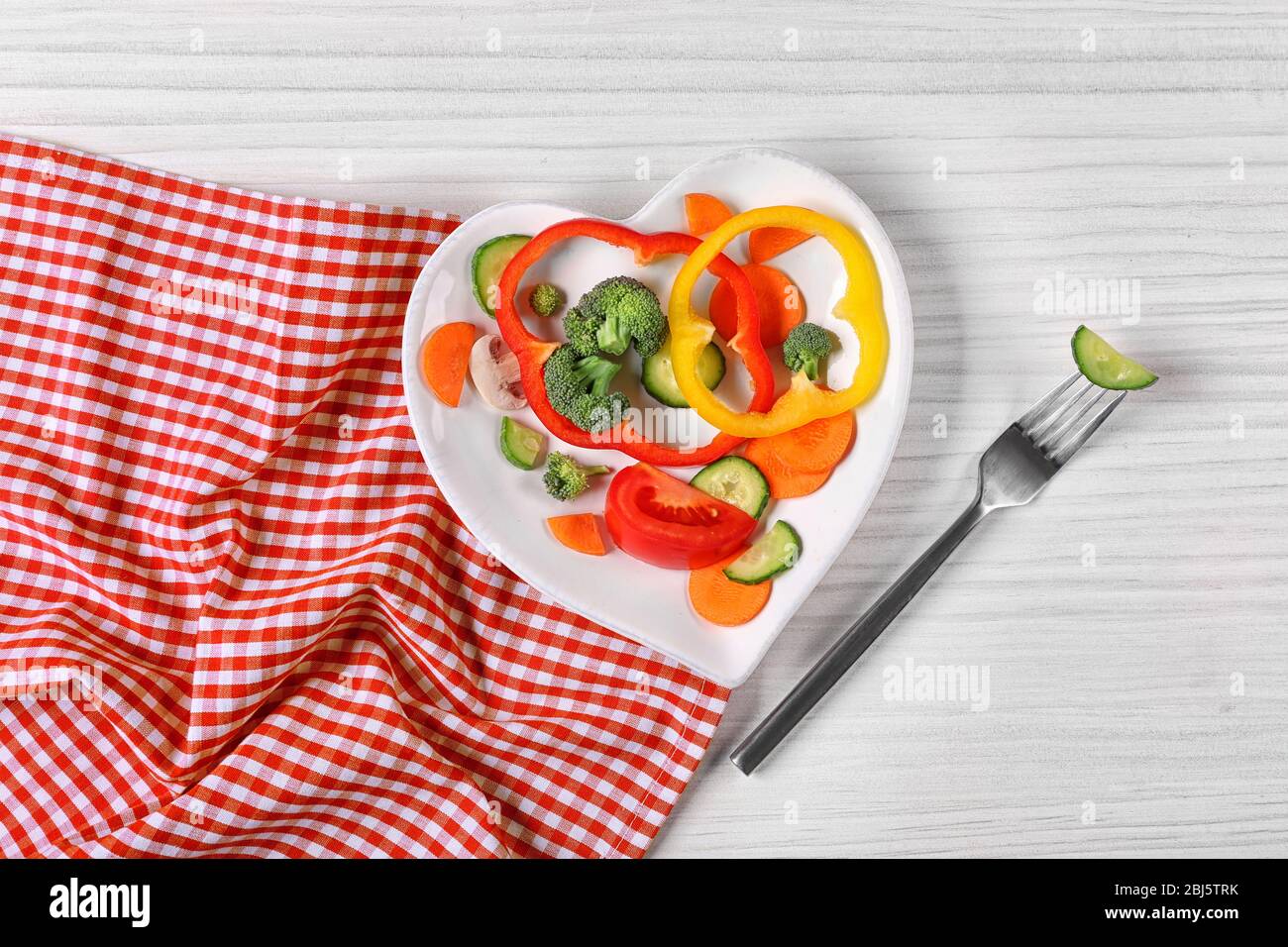 Useful cut vegetables on a plate in the form of heart on wooden table ...