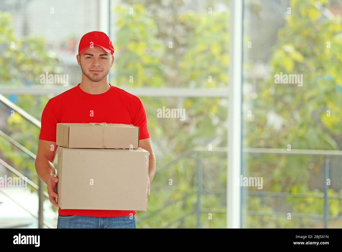 Delivery concept - postman in red uniform holding package near stairs ...