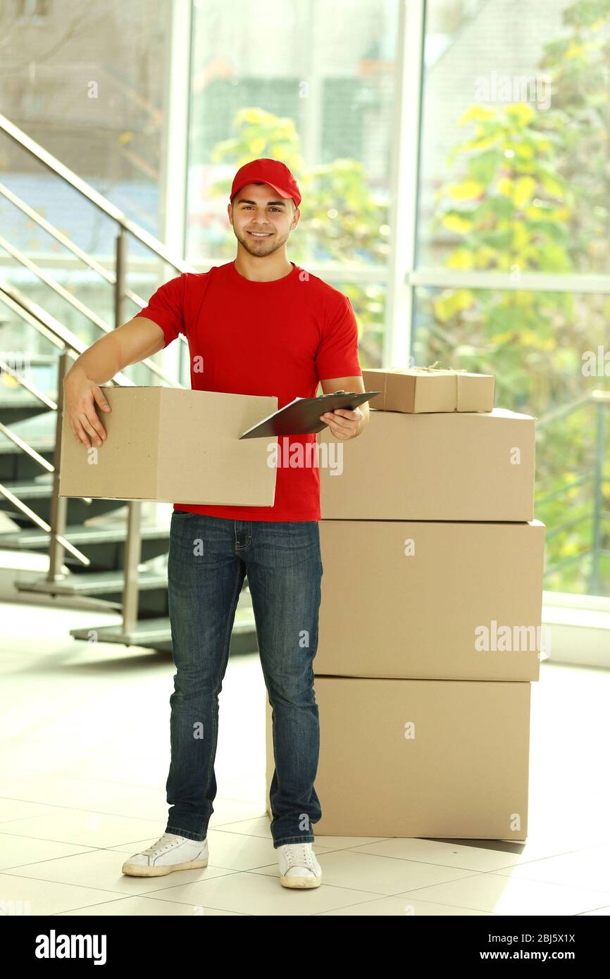 Delivery concept - postman in red uniform holding package near stairs ...
