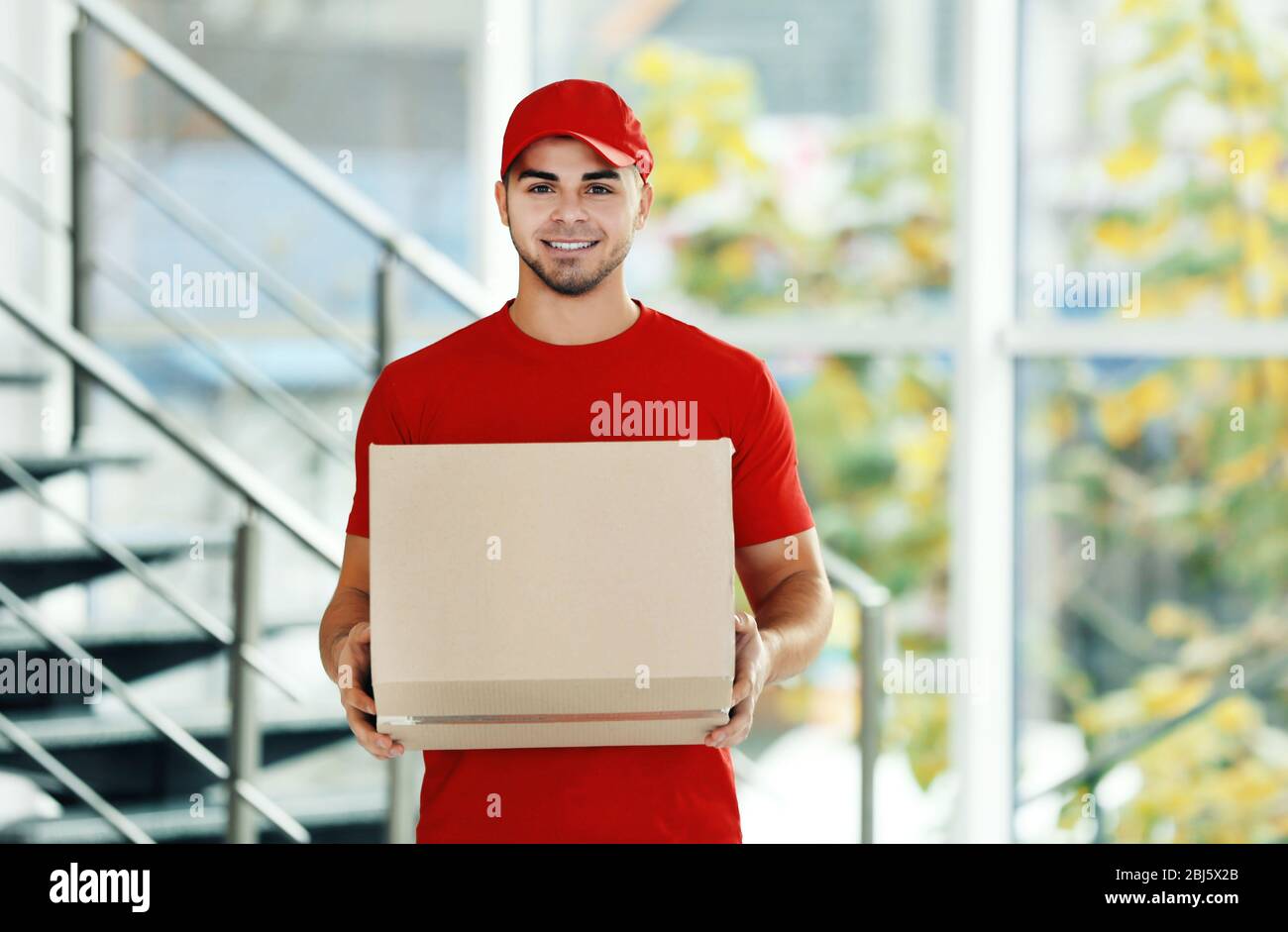 Delivery concept - postman in red uniform holding package near stairs ...