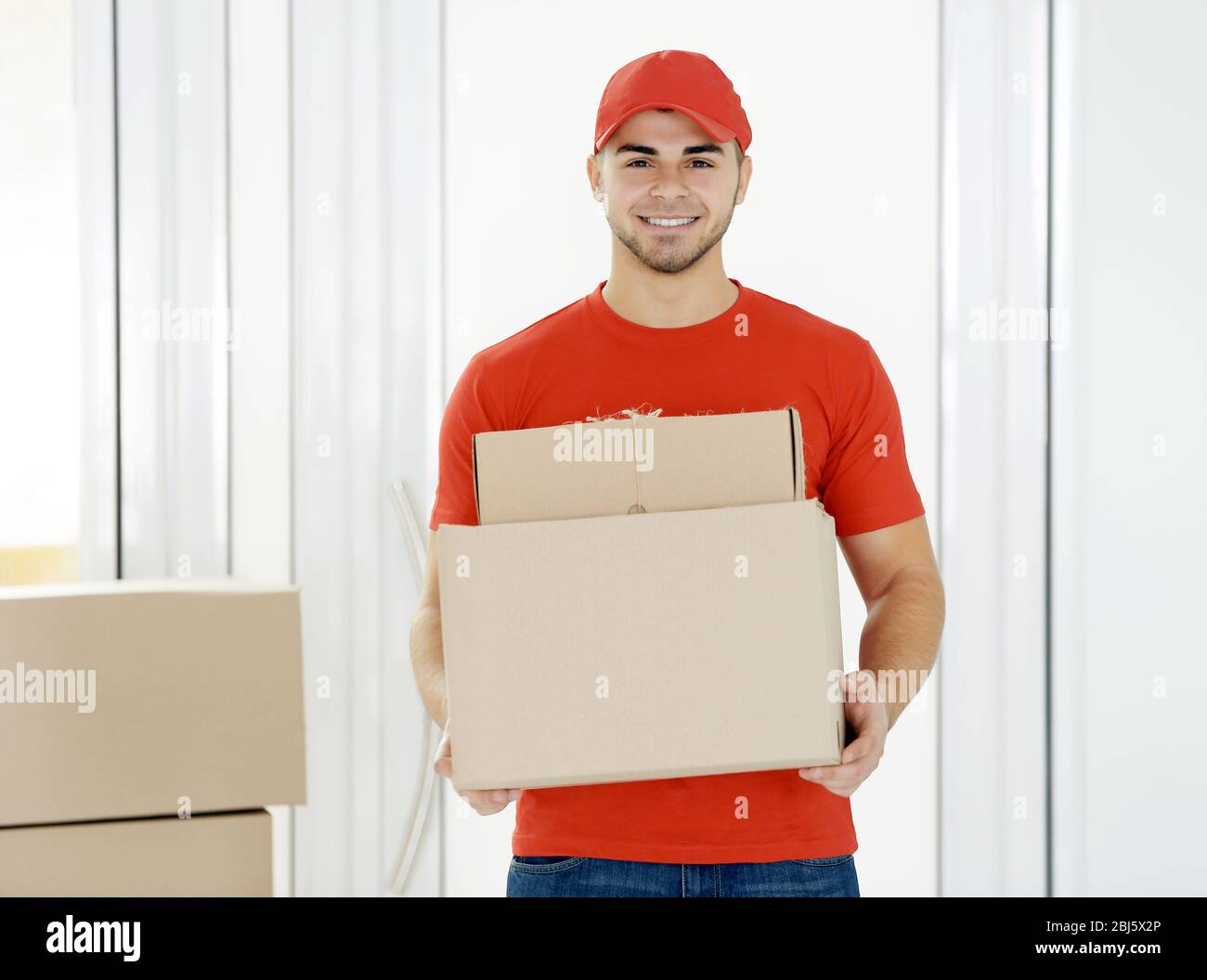Delivery man in red uniform holding package Stock Photo - Alamy