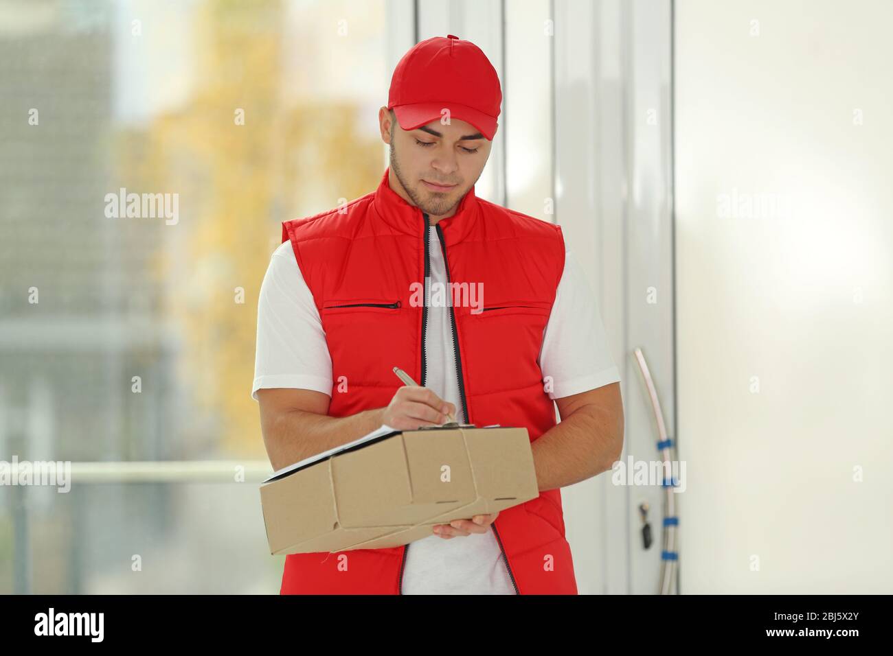 Delivery man in red uniform holding package Stock Photo - Alamy