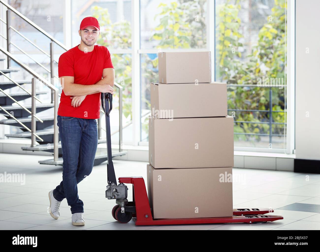 Delivery concept - postman in red uniform with parcels on dolly Stock ...