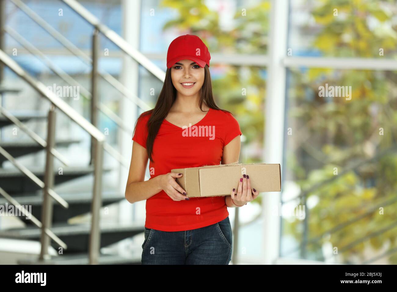 Delivery woman in red uniform holding package near stairs Stock Photo ...