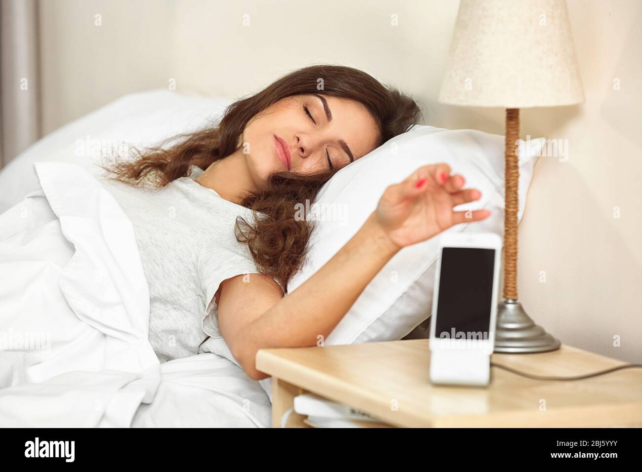 Beautiful young woman waking up with mobile alarm clock Stock Photo - Alamy