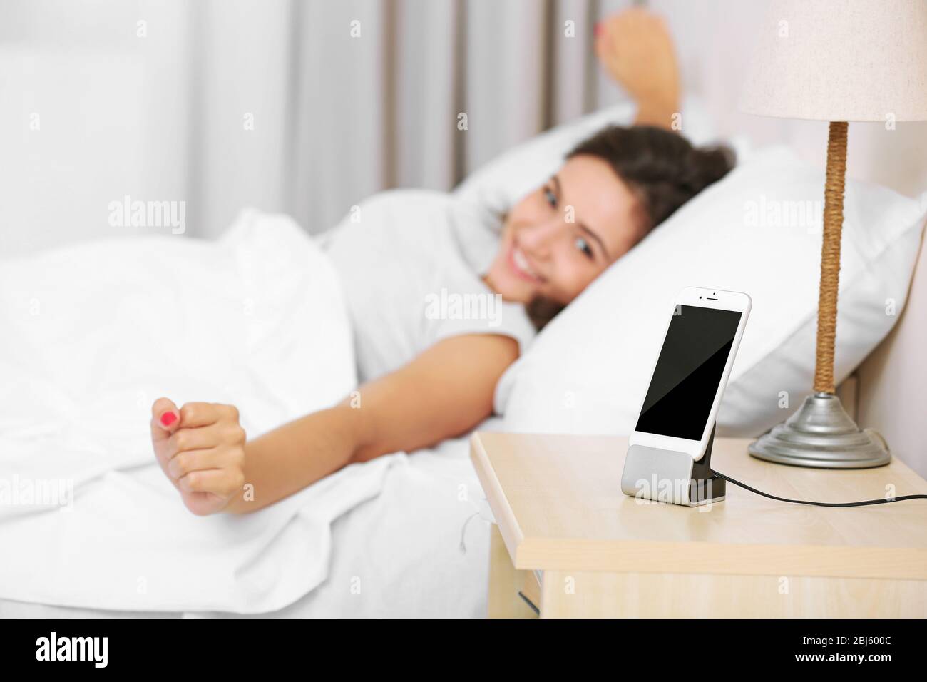 Beautiful young woman waking up with mobile alarm clock Stock Photo - Alamy