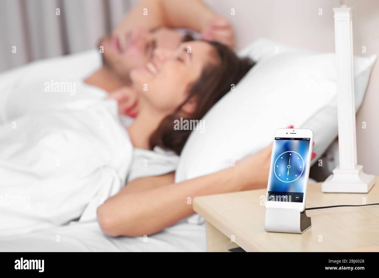 Happy couple waking up with mobile alarm clock Stock Photo - Alamy