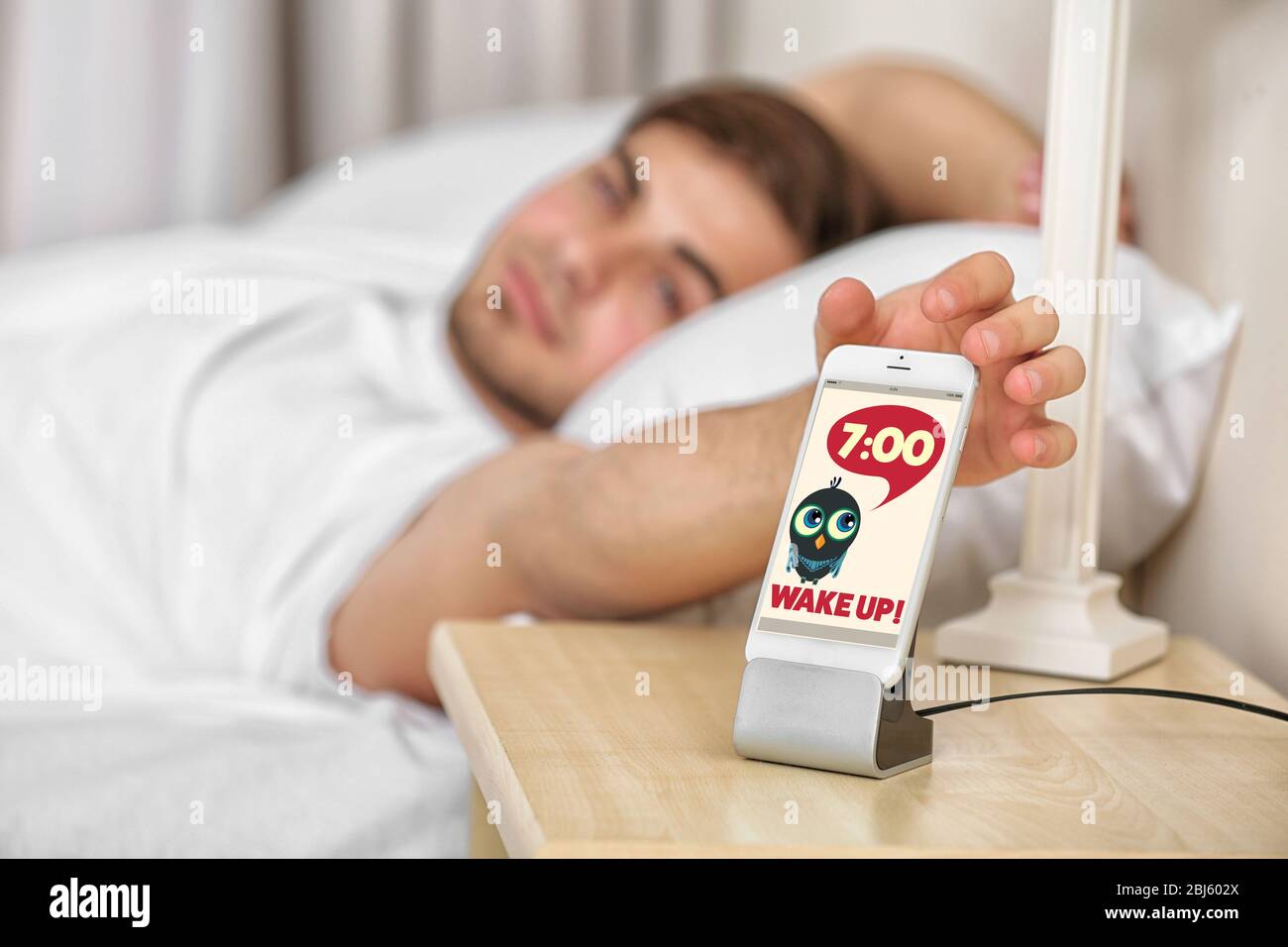 Beautiful young man waking up with mobile alarm clock Stock Photo - Alamy
