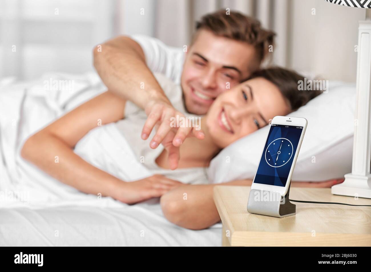 Happy couple waking up with mobile alarm clock Stock Photo - Alamy