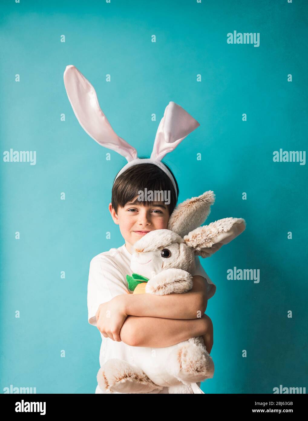 Boy wearing bunny ears hugging toy rabbit against blue background Stock ...