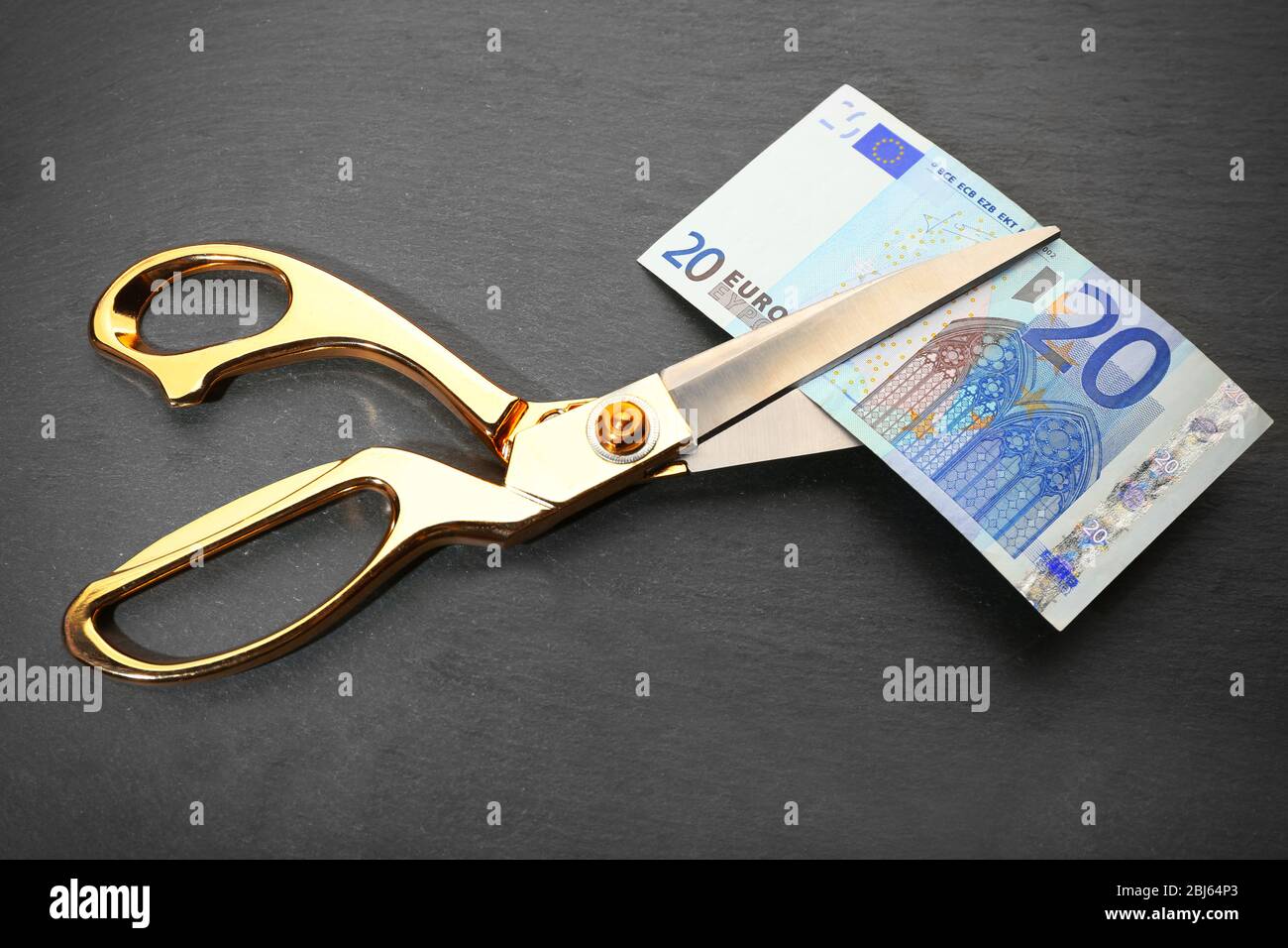 Golden scissors cut money on black background Stock Photo - Alamy