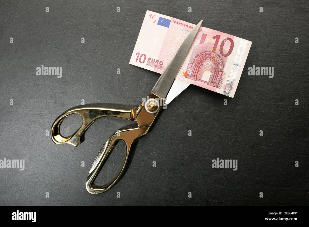 Golden scissors cut money on black background Stock Photo - Alamy