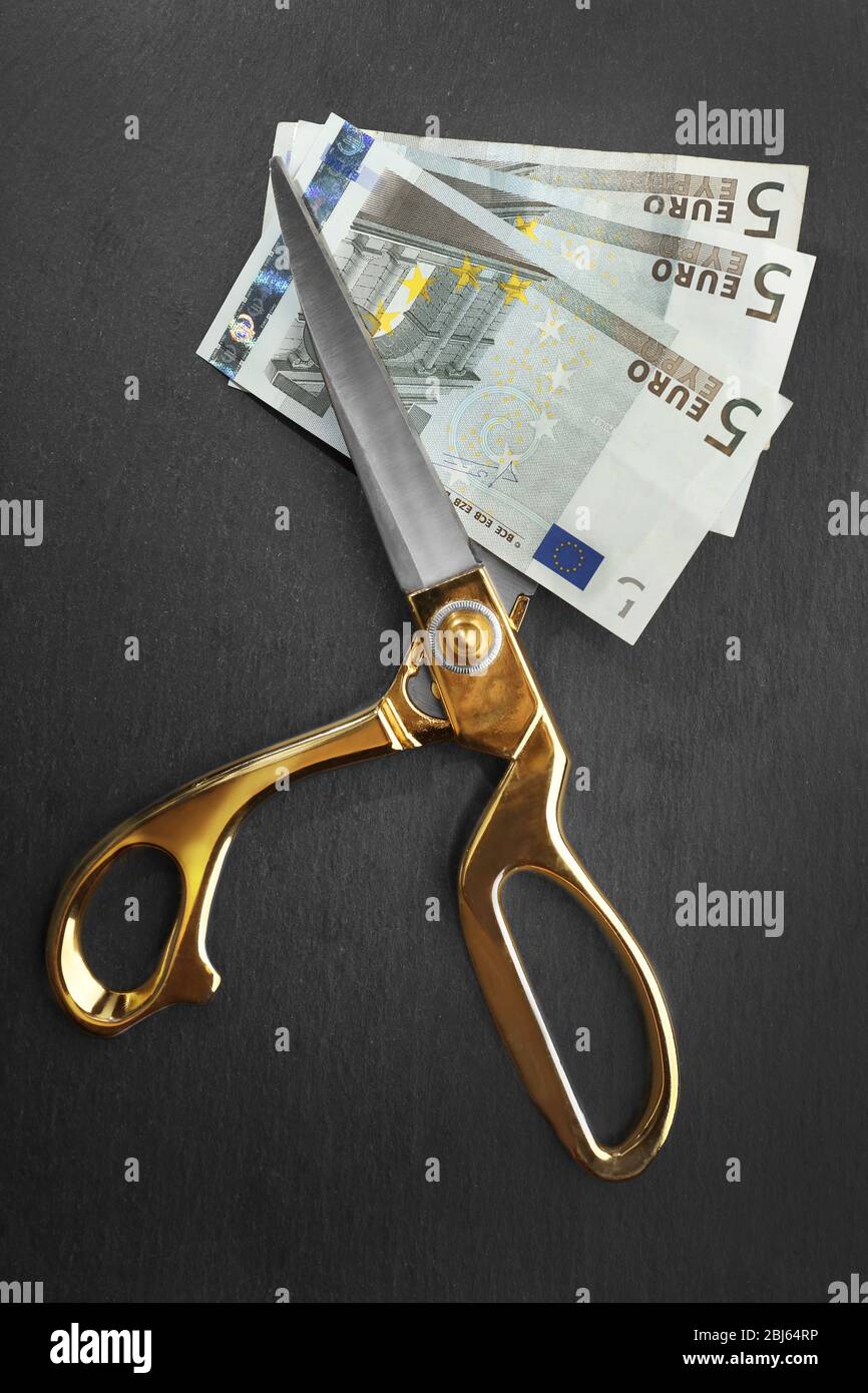 Golden scissors cut money on black background Stock Photo - Alamy