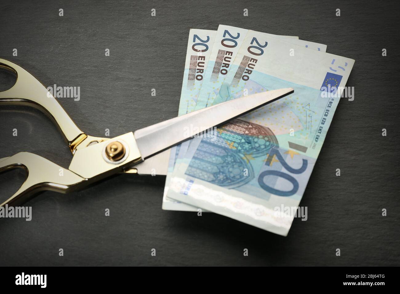 Golden scissors cut money on black background Stock Photo - Alamy