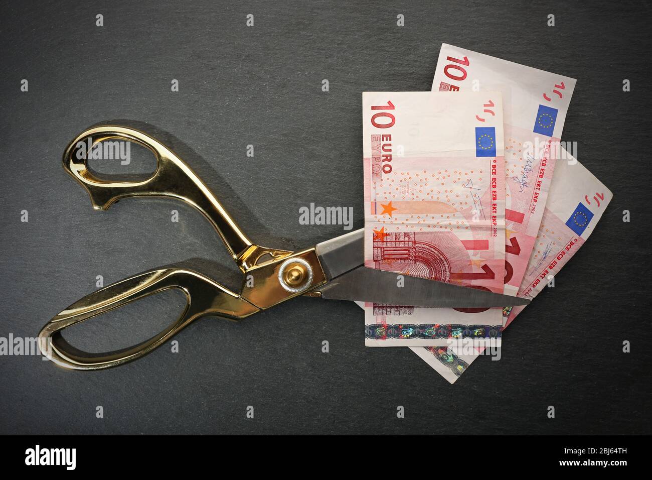 Golden scissors cut money on black background Stock Photo - Alamy