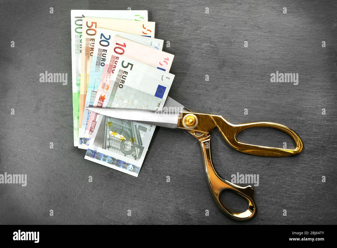Golden scissors cut money on black background Stock Photo - Alamy