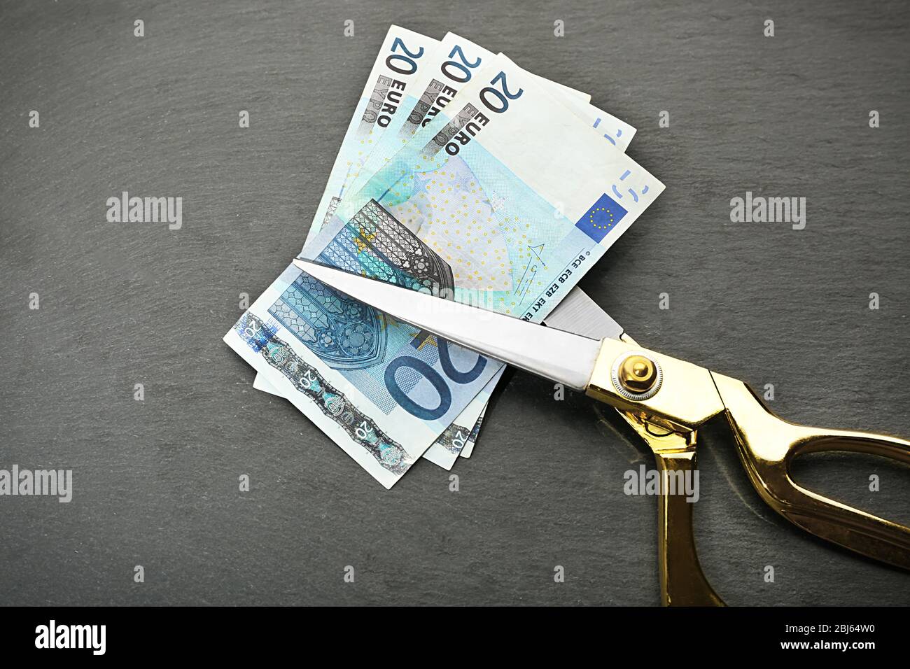 Golden scissors cut money on black background Stock Photo - Alamy