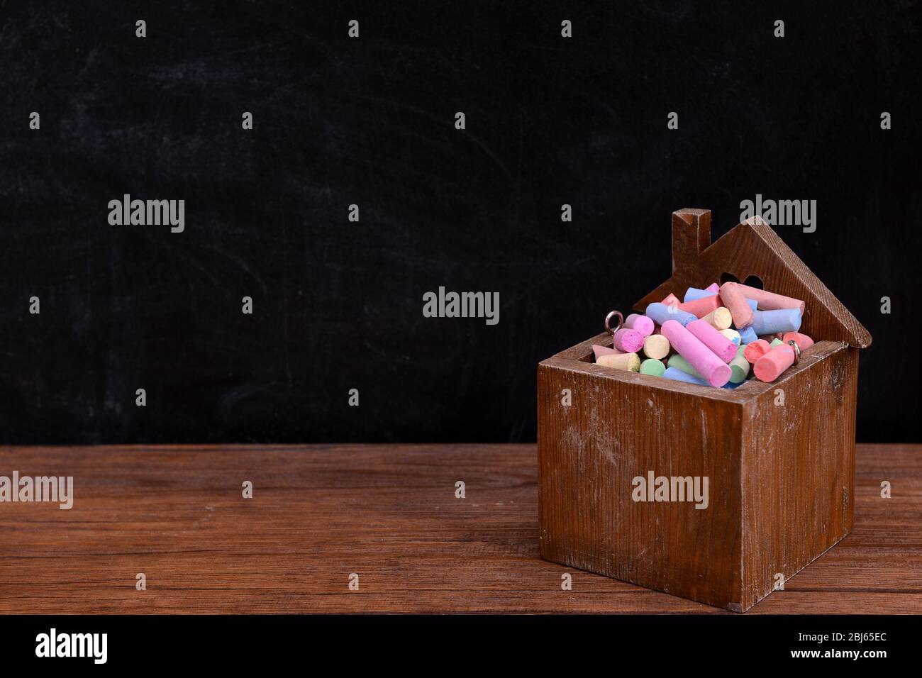 House shaped wooden box of coloured chalk in front of blackboard Stock ...