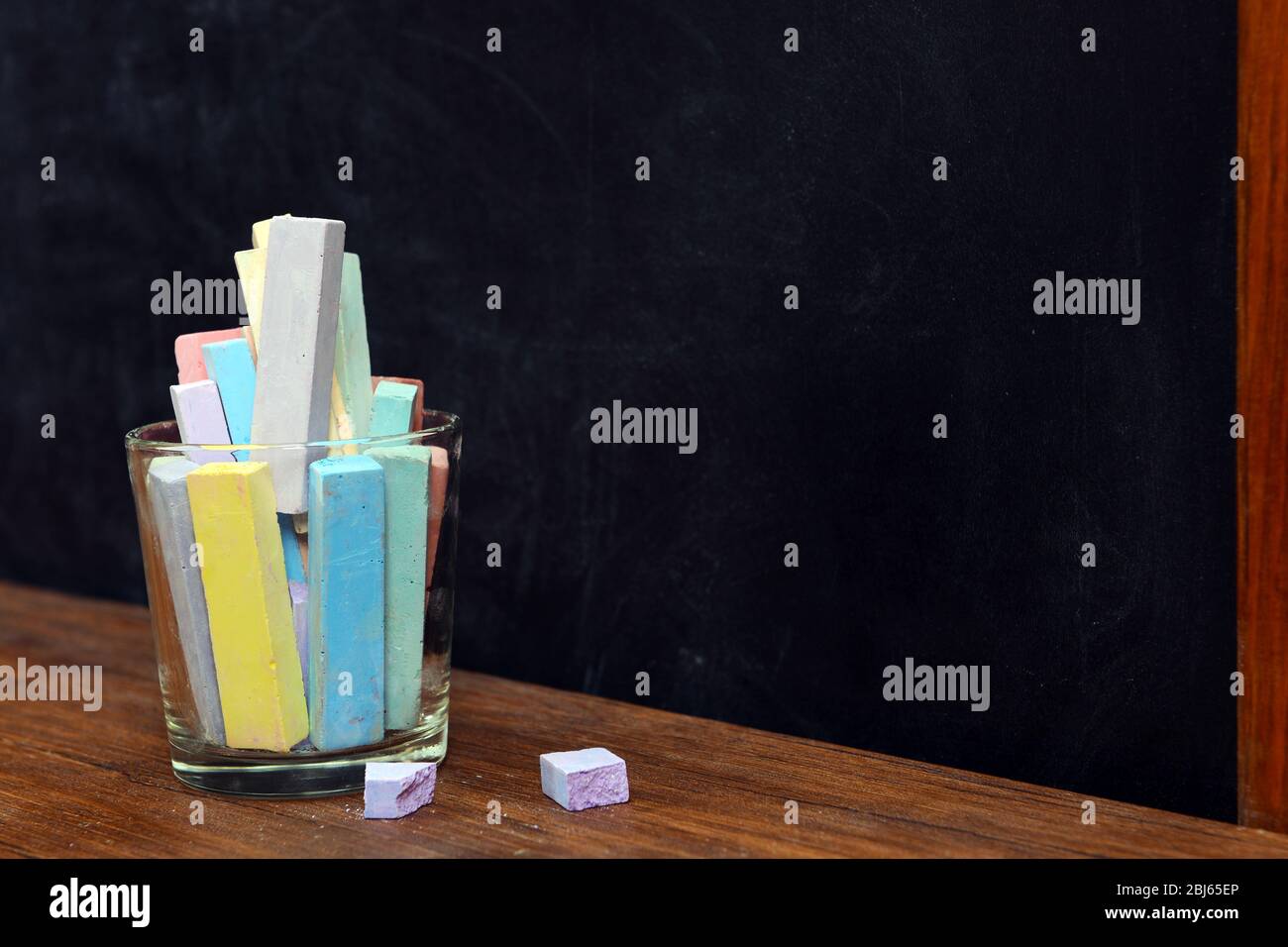 Glass of coloured chalk on desk in front of blackboard Stock Photo - Alamy