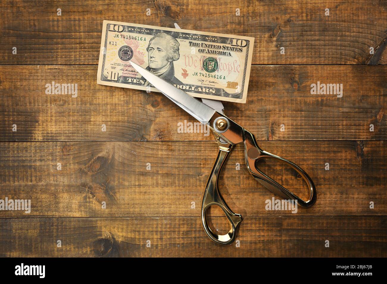 Scissors cuts dollar banknote on wooden background Stock Photo - Alamy