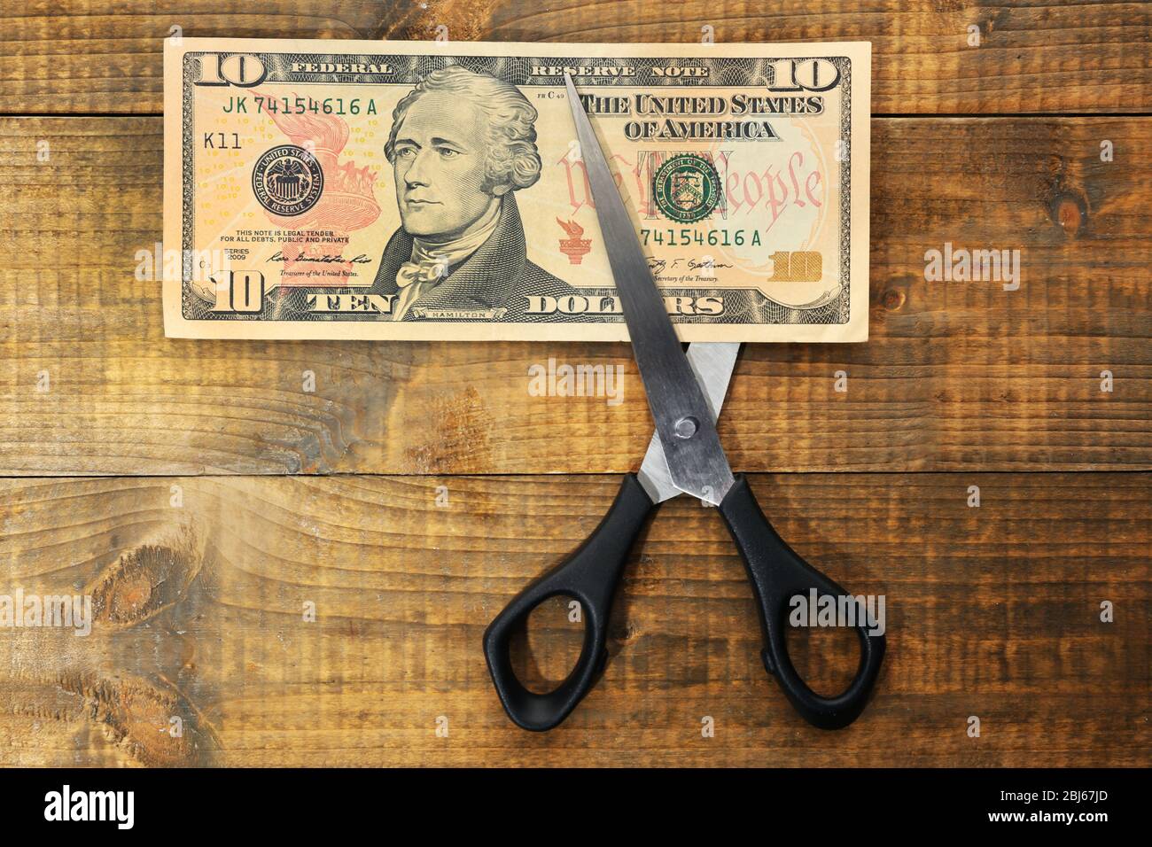 Scissors cuts dollar banknote on wooden background Stock Photo - Alamy