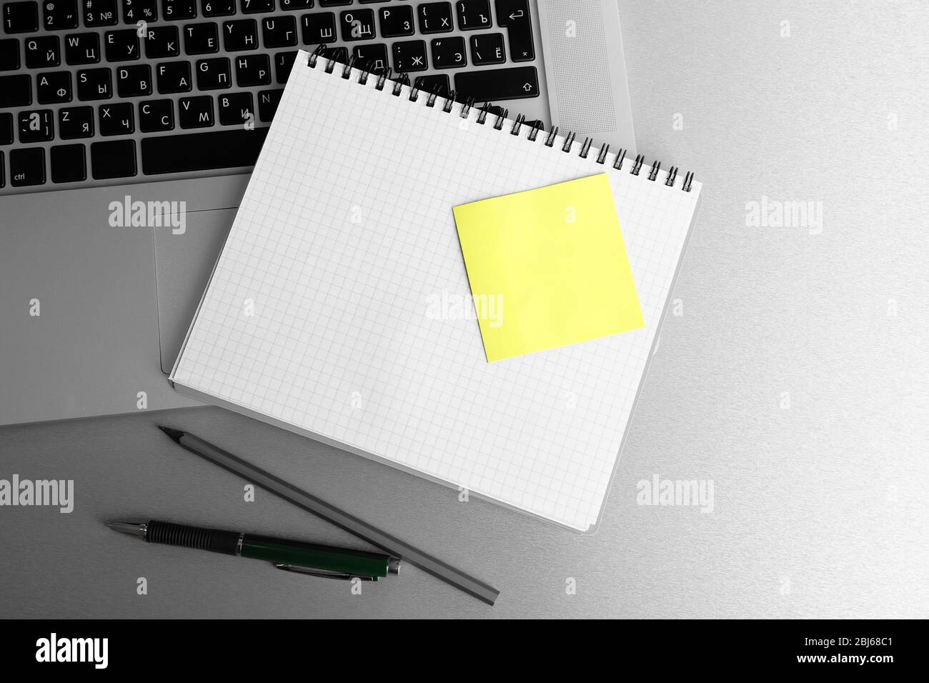 Empty yellow adhesive paper, notebook on laptop keyboard, pen and ...