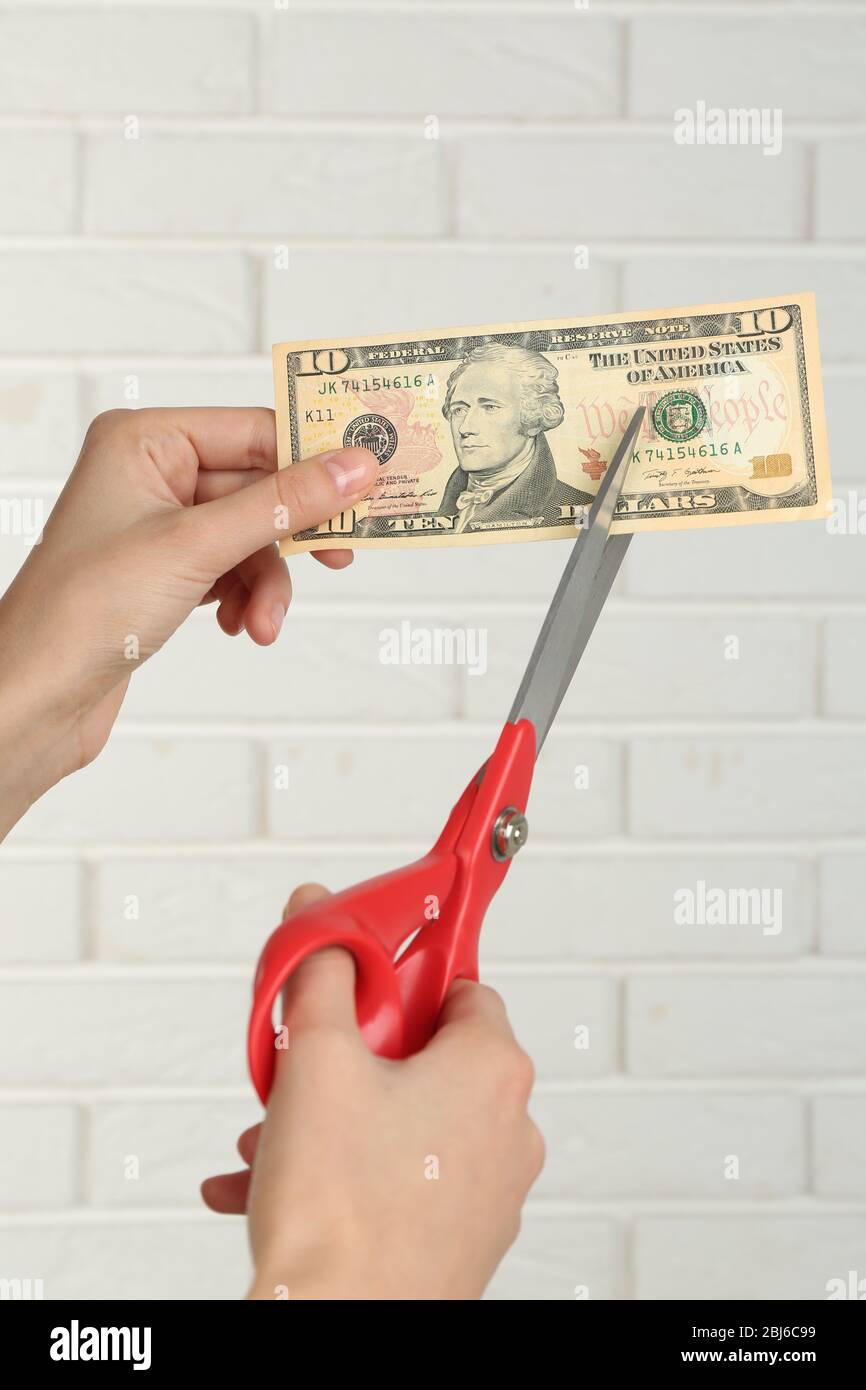 Hands with scissors cutting money on white brick wall background Stock ...
