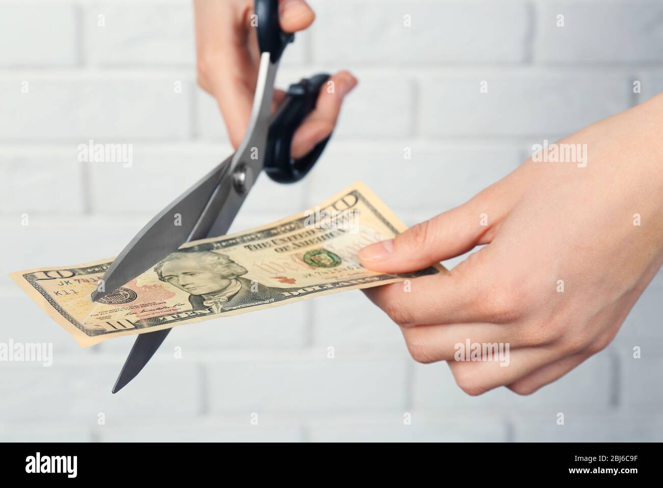 Hands with scissors cutting money on white brick wall background Stock ...