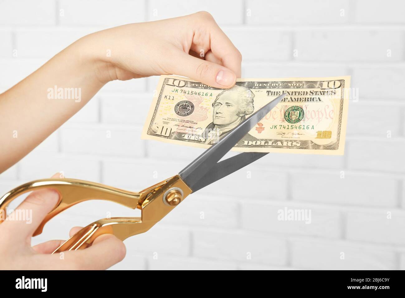 Hands with scissors cutting money on white brick wall background Stock ...