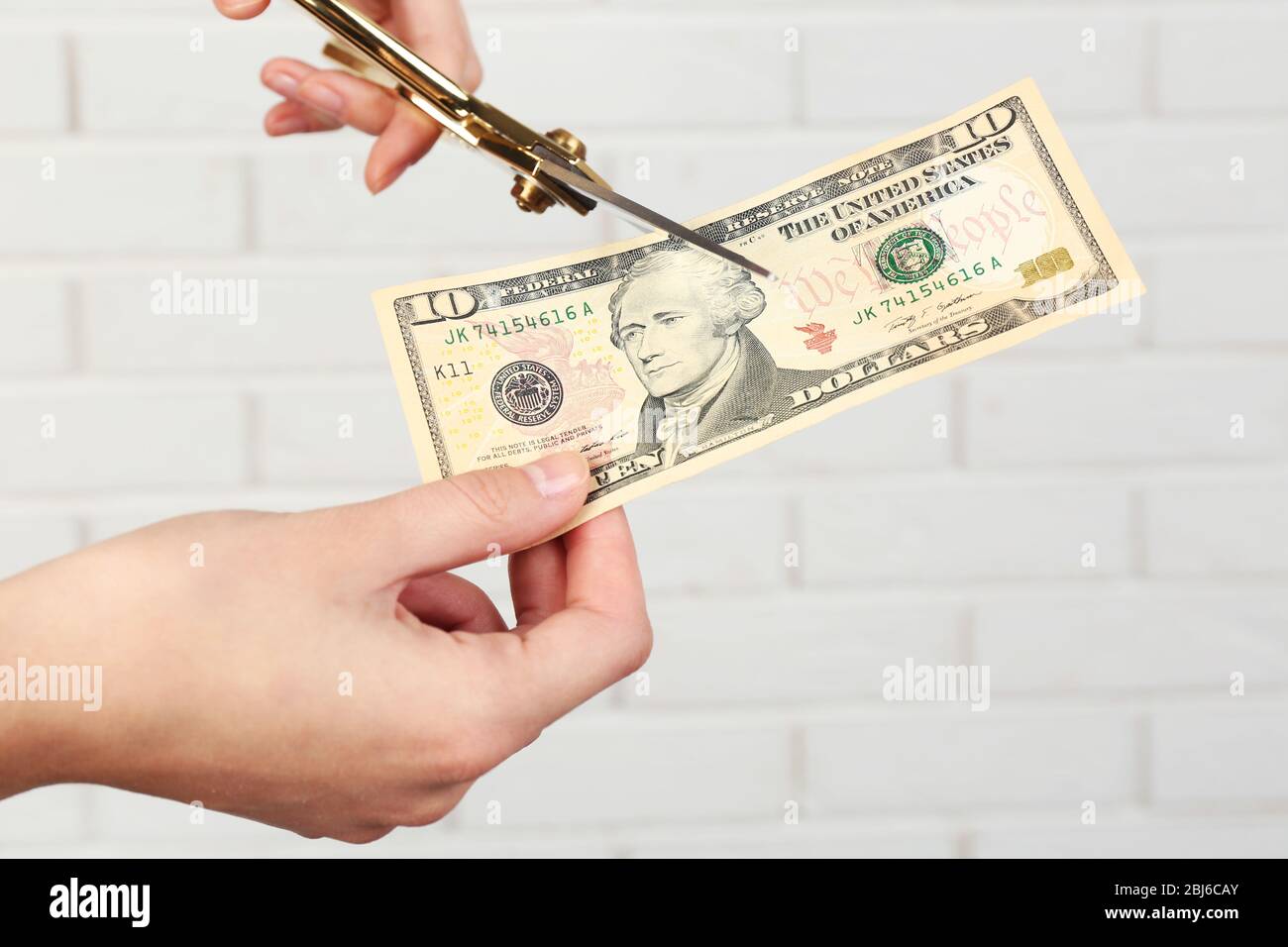 Hands with scissors cutting money on white brick wall background Stock ...
