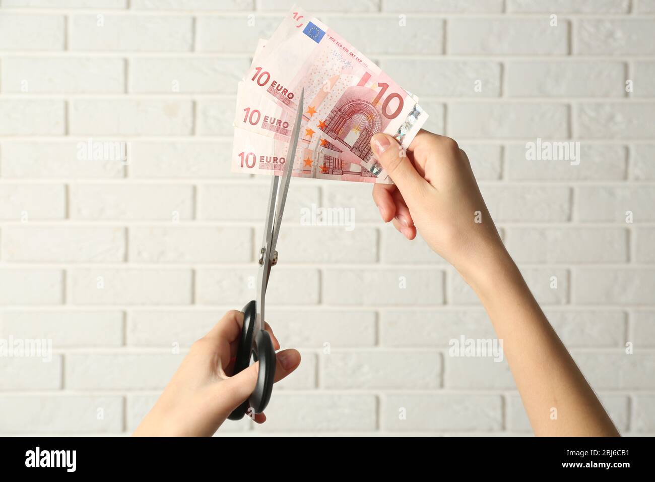 Hands with scissors cutting money on white brick wall background Stock ...