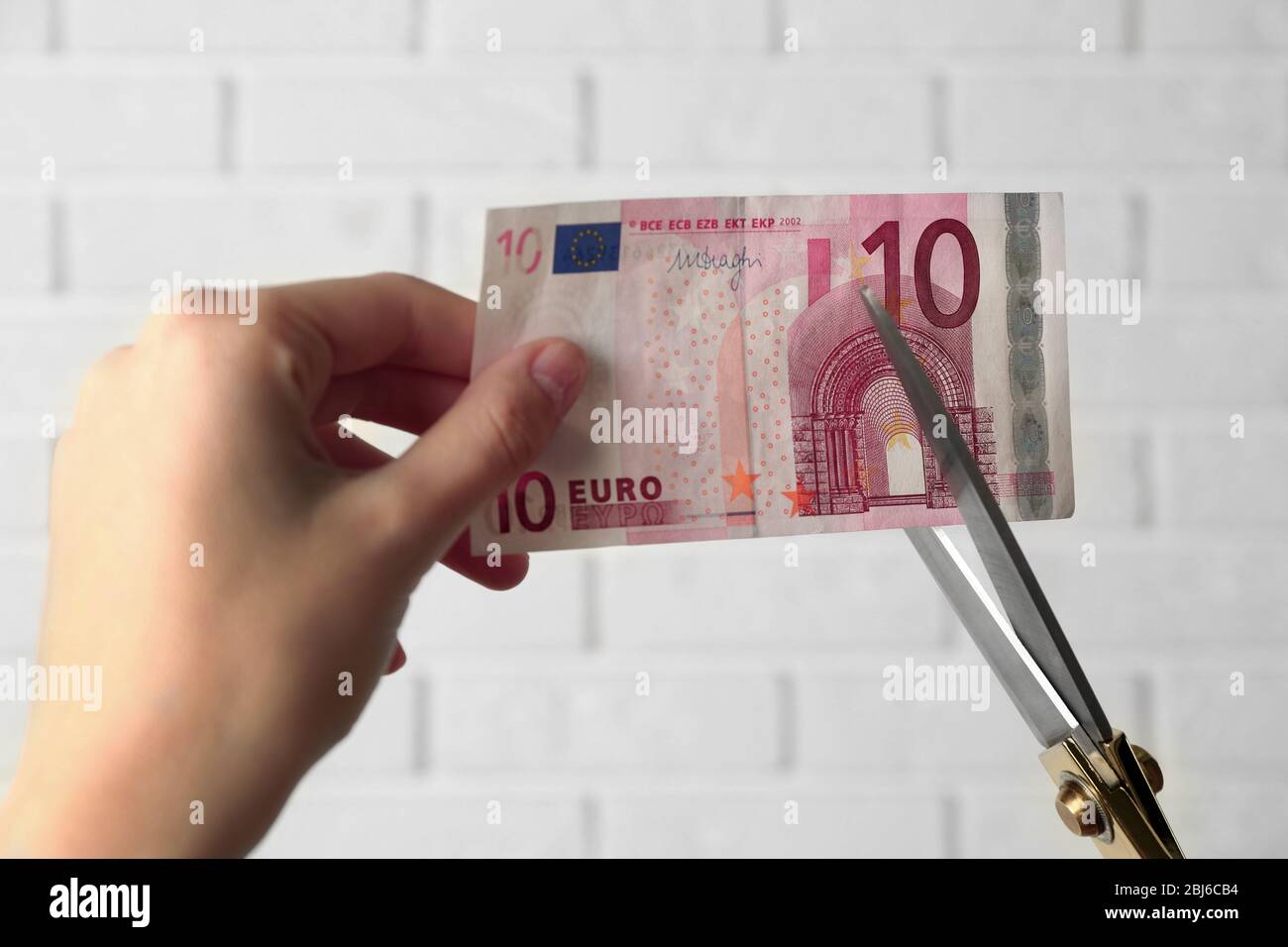 Hands with scissors cutting money on white brick wall background Stock ...