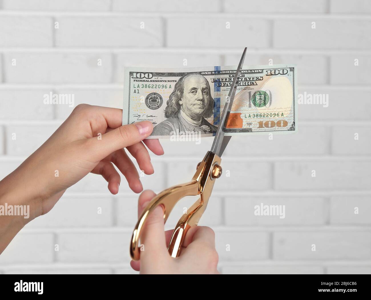 Hands with scissors cutting money on white brick wall background Stock ...