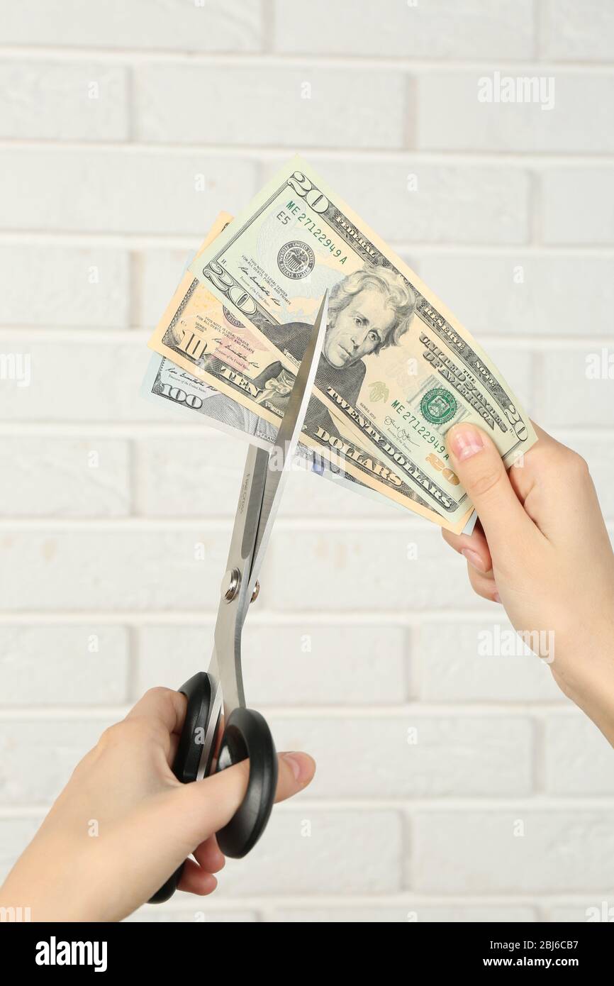 Hands with scissors cutting money on white brick wall background Stock ...