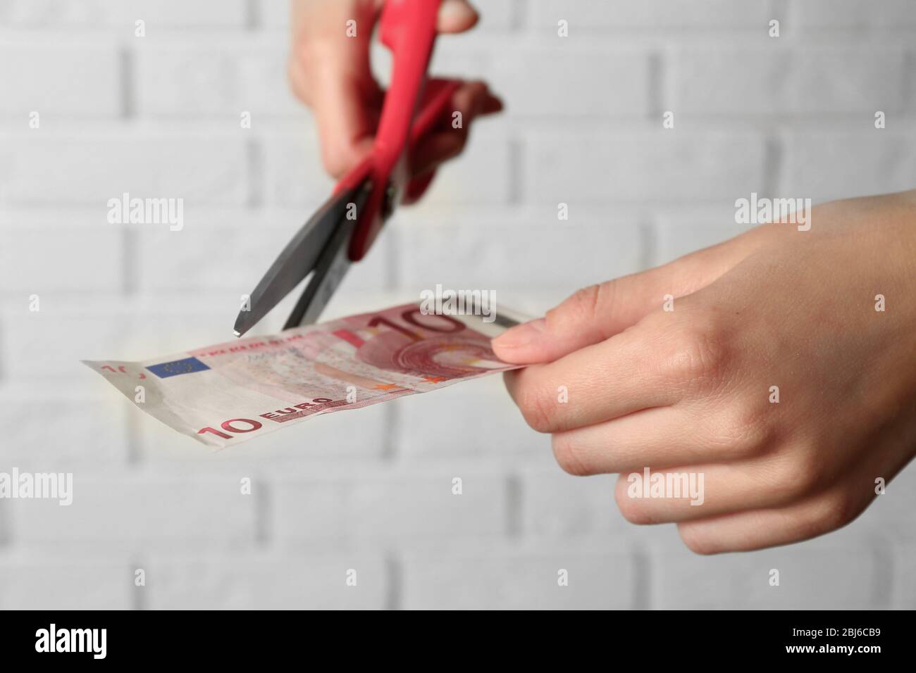 Hands with scissors cutting money on white brick wall background Stock ...