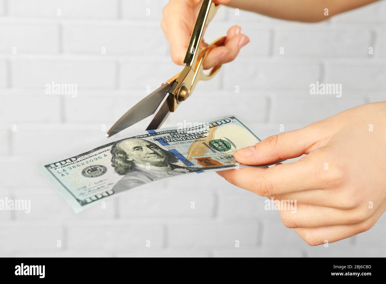 Hands with scissors cutting money on white brick wall background Stock ...