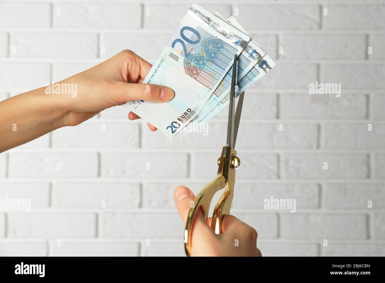 Hands with scissors cutting money on white brick wall background Stock ...