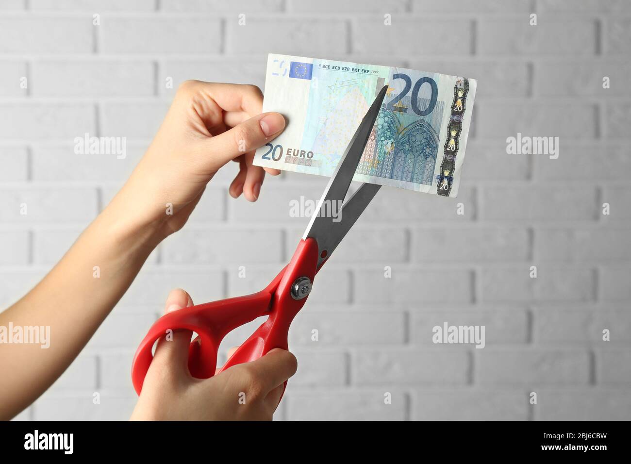 Hands with scissors cutting money on white brick wall background Stock ...