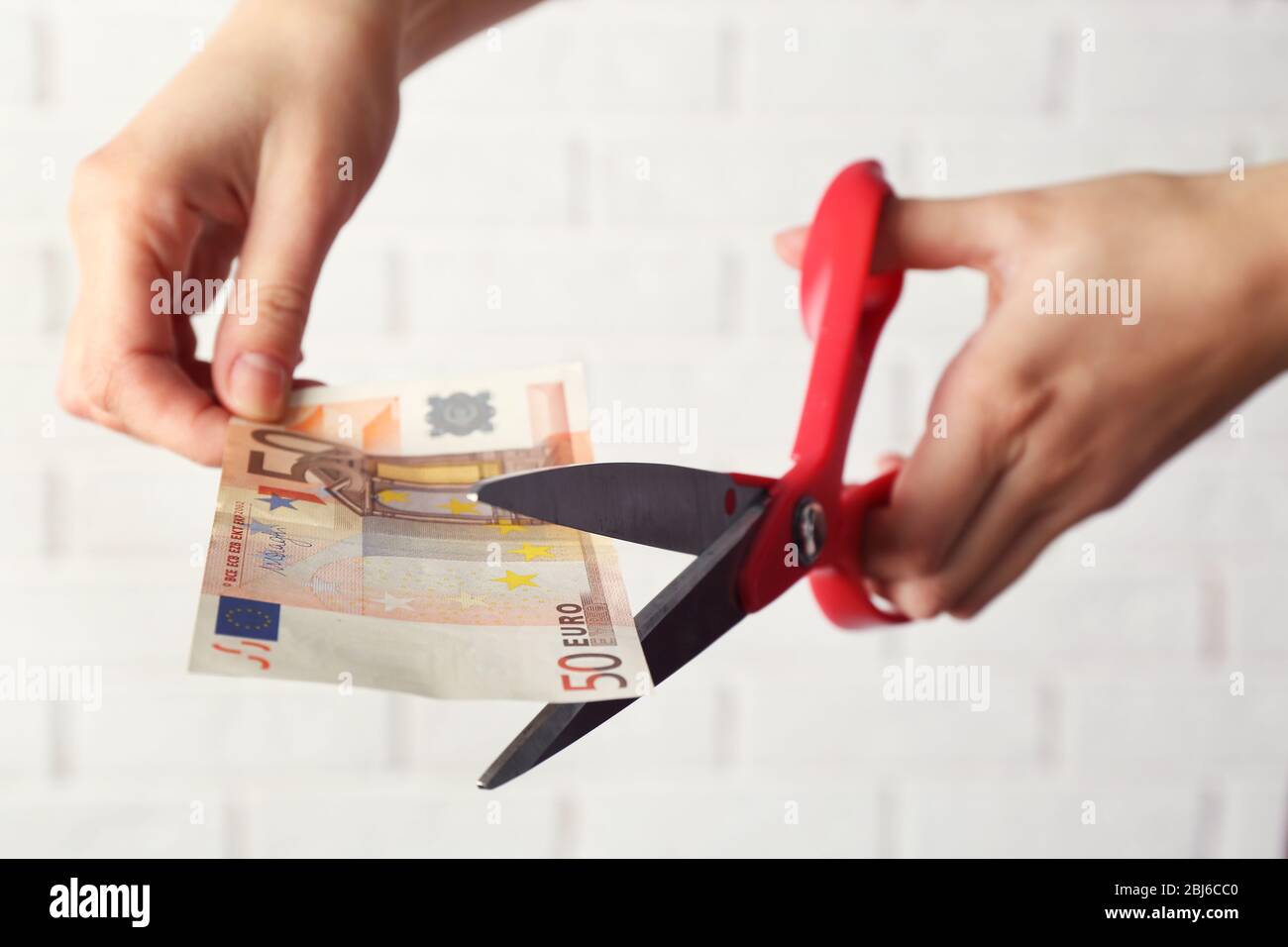 Hands with scissors cutting money on white brick wall background Stock ...