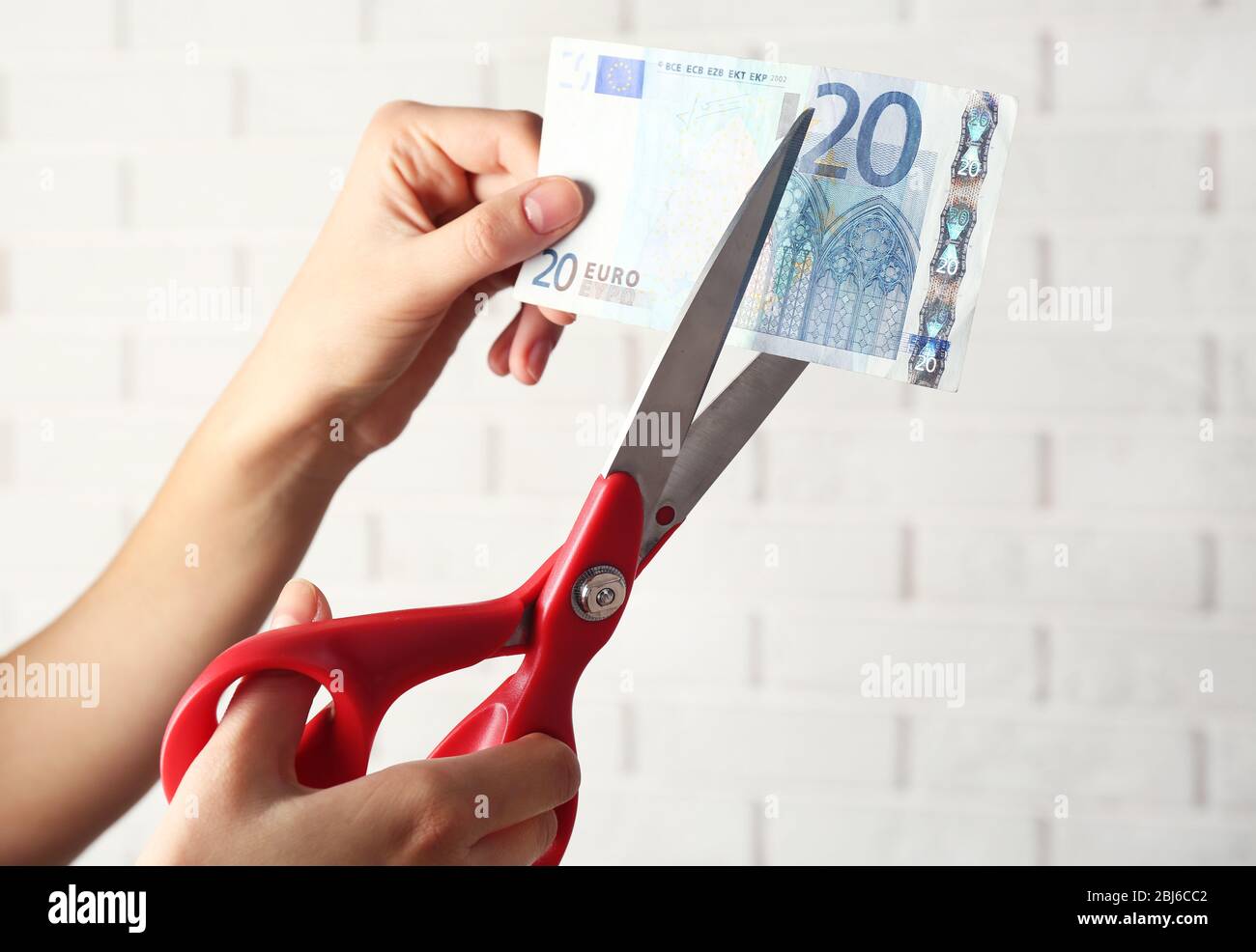 Hands with scissors cutting money on white brick wall background Stock ...