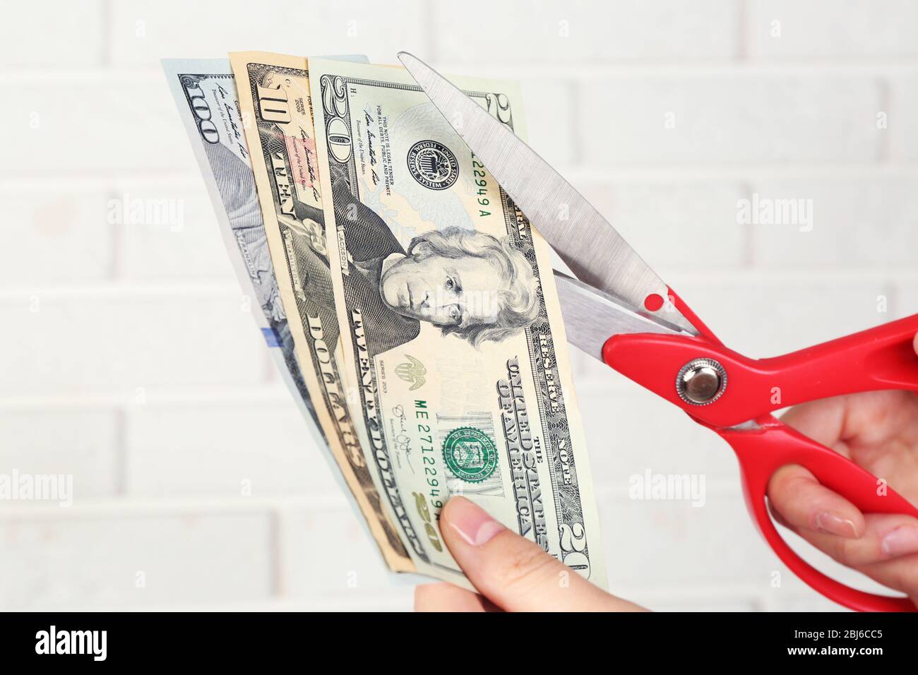 Hands with scissors cutting money on white brick wall background Stock ...