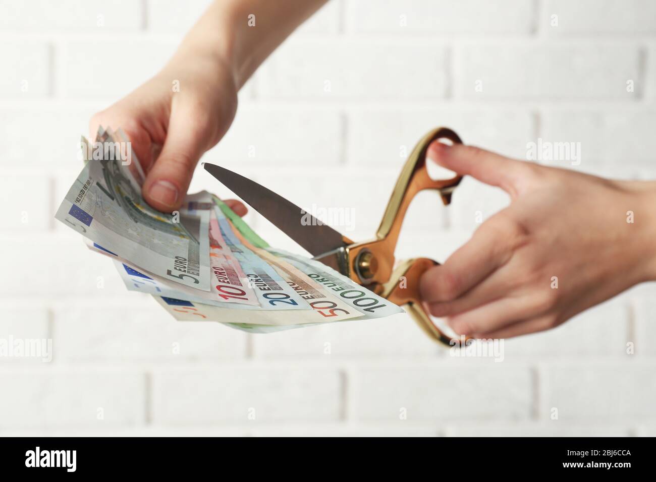 Hands with scissors cutting money on white brick wall background Stock ...