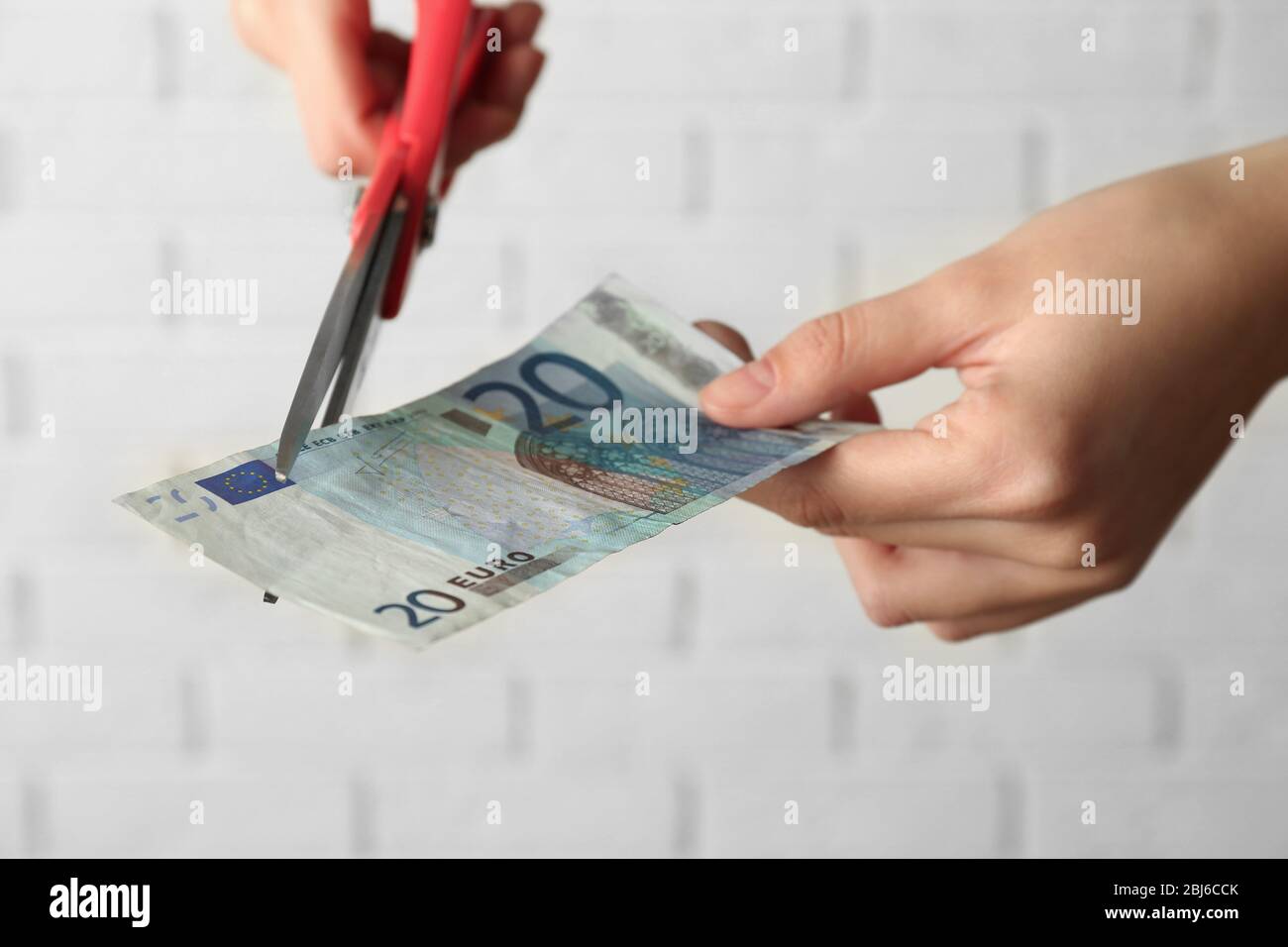 Hands with scissors cutting money on white brick wall background Stock ...
