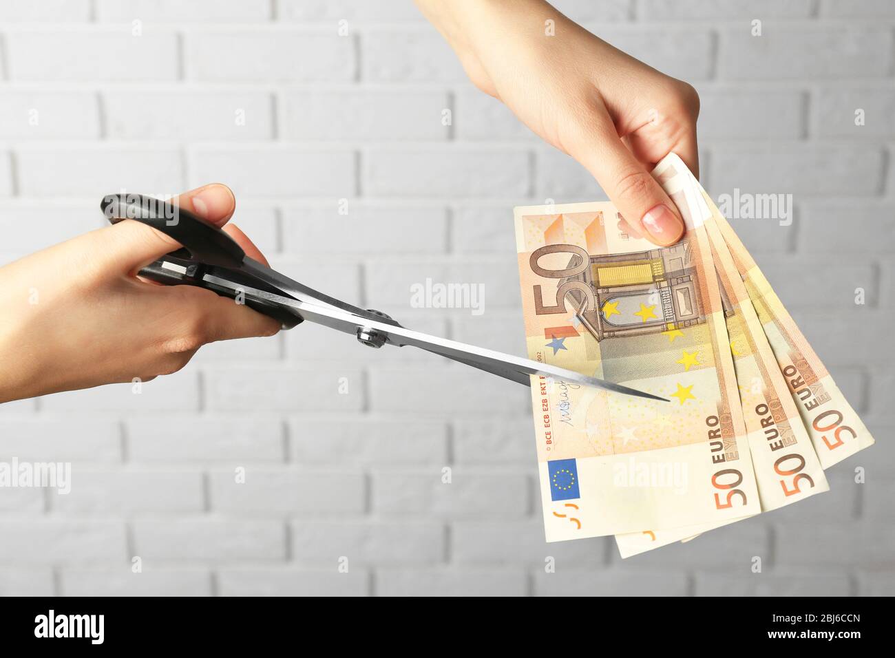 Hands with scissors cutting money on white brick wall background Stock ...