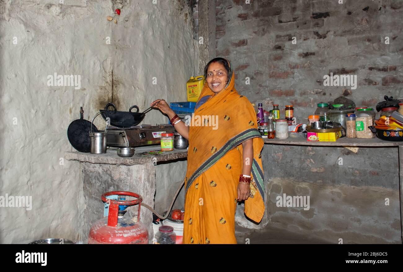 Happy rural woman standing in kitchen, cooking food on gas stove, India ...