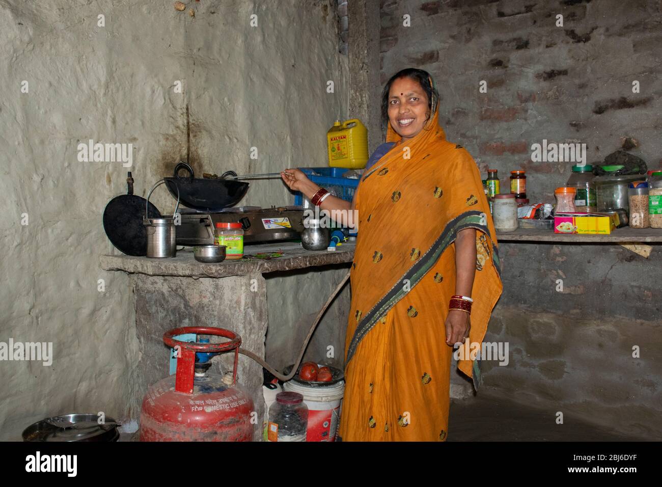 Happy rural woman standing in kitchen, cooking food on gas stove, India ...